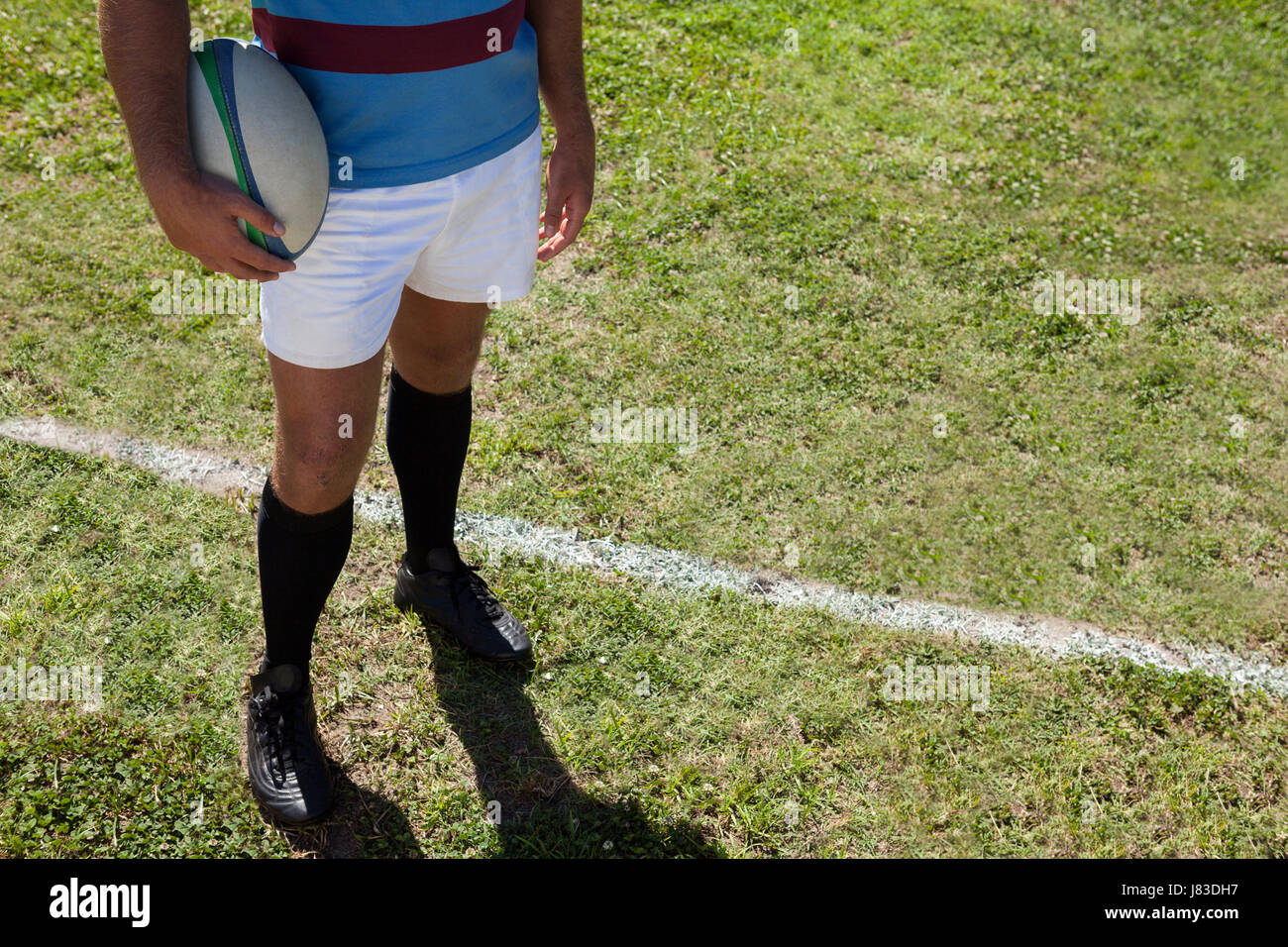 Low section of rugby player with ball standing on field during sunny ...