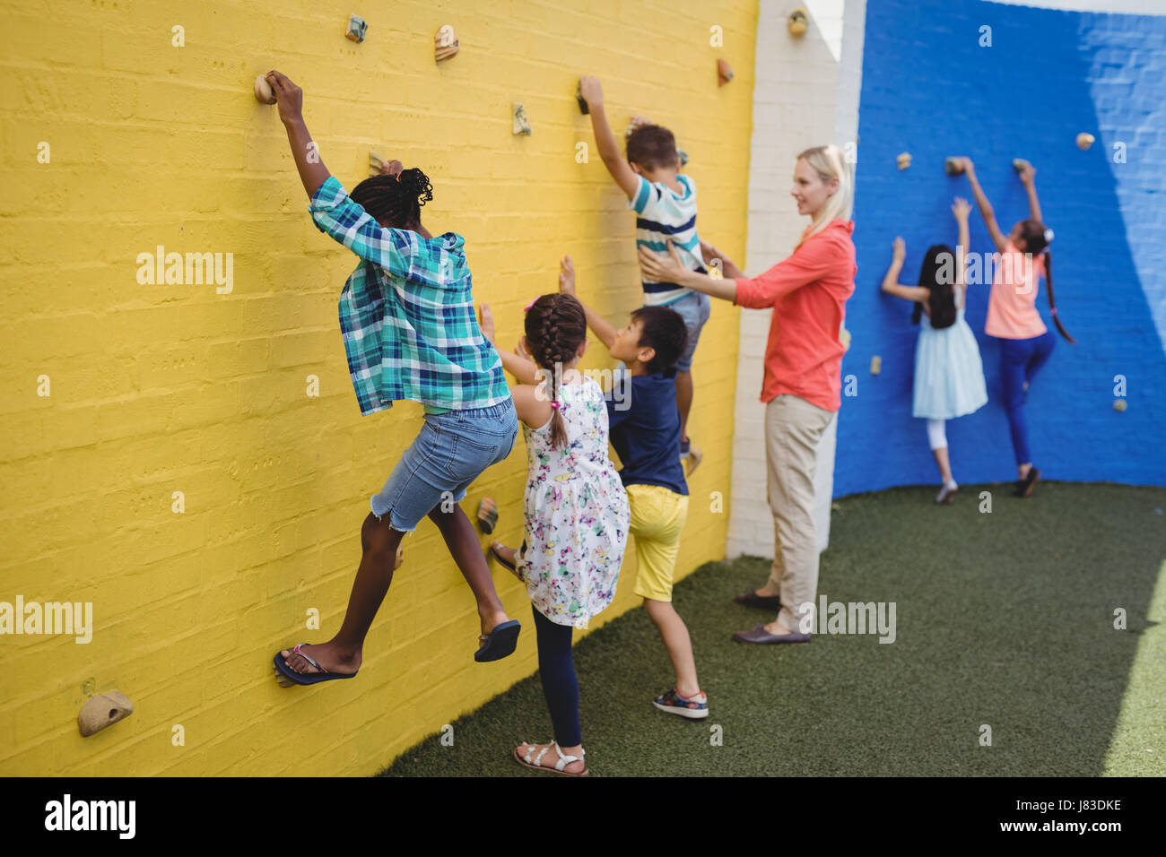 Trainer assisting kids in climbing wall in school Stock Photo - Alamy