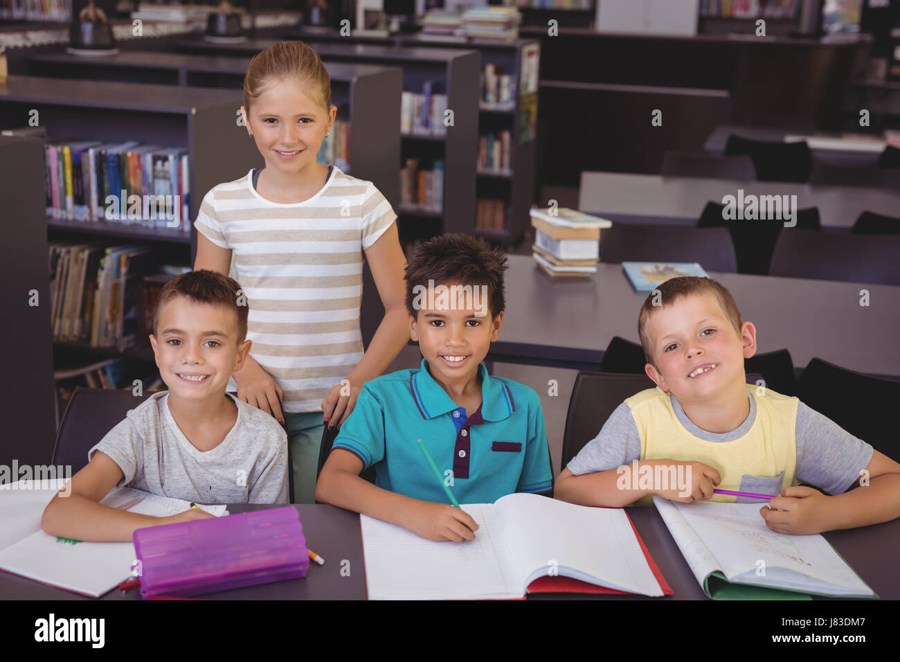 Portrait of smiling schoolkids doing their homework in library at ...