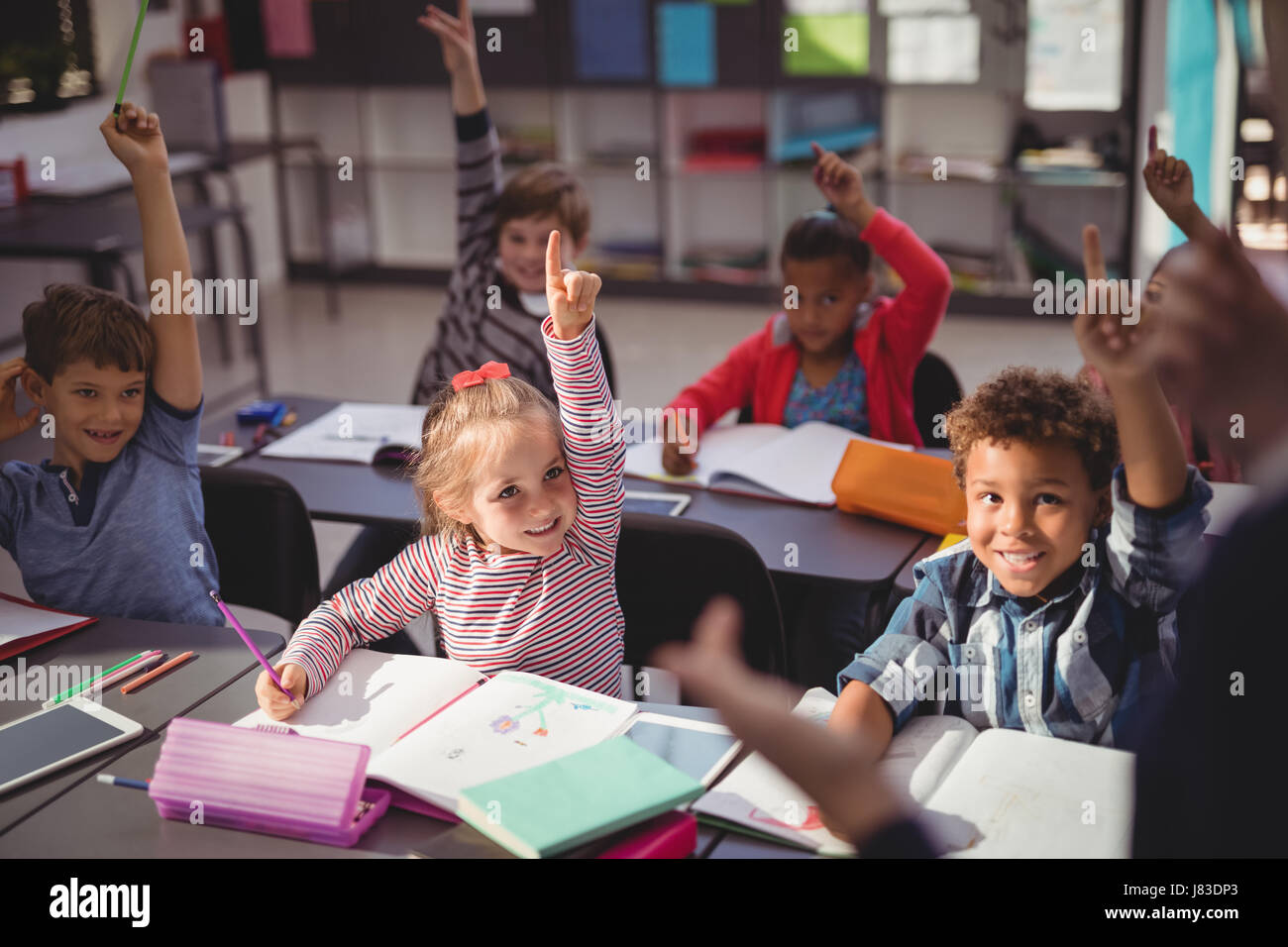 Schoolkids raising their hands in classroom at school Stock Photo - Alamy