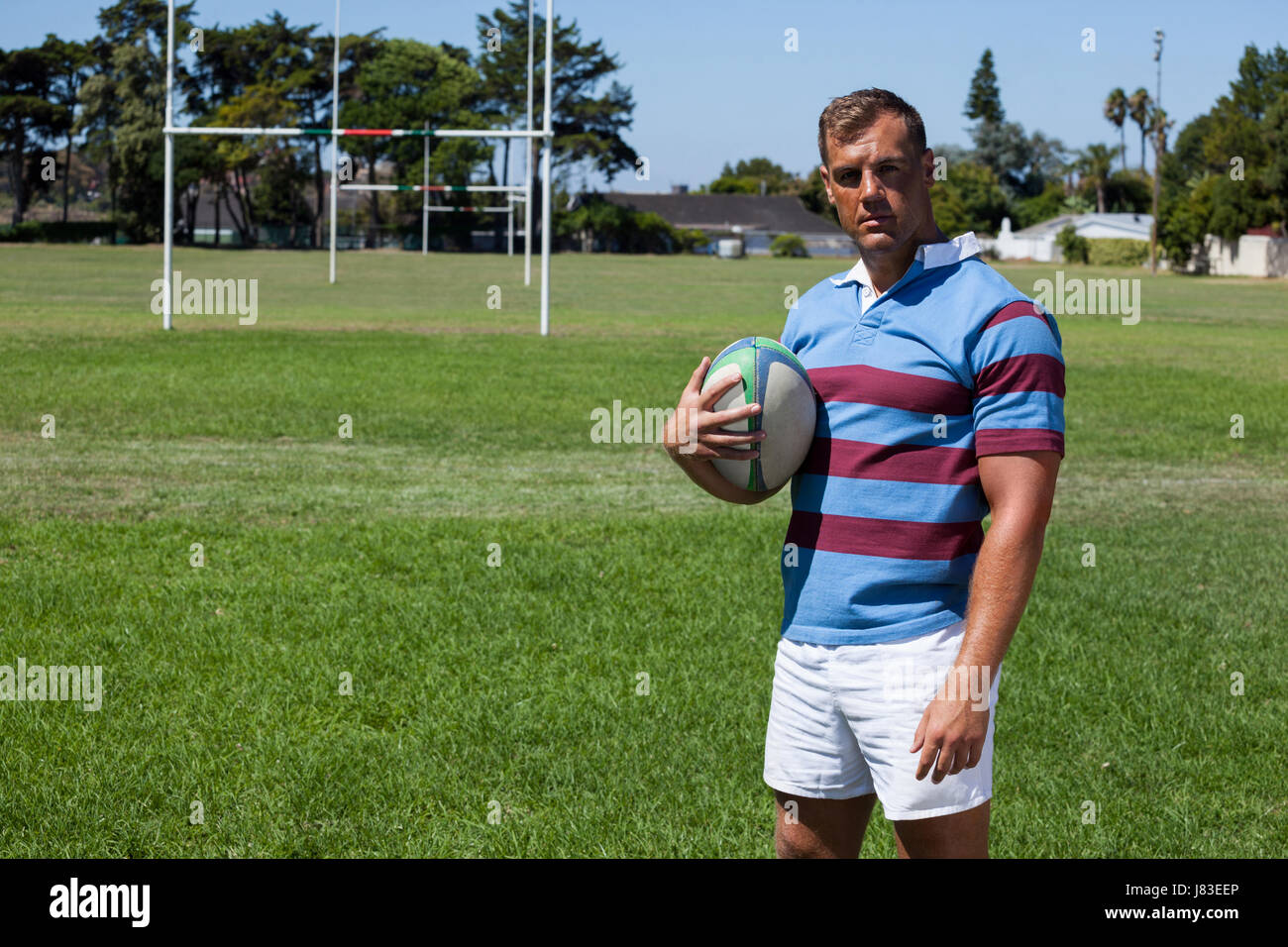 Portrait of confident rugby player holding ball while standing against ...