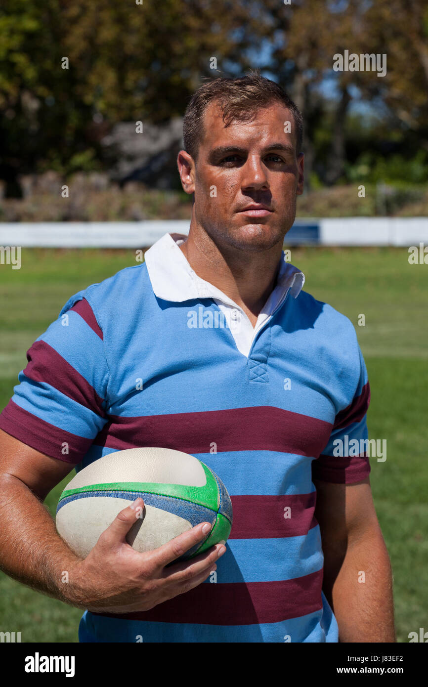 Confident rugby player holding ball while standing on field Stock Photo ...