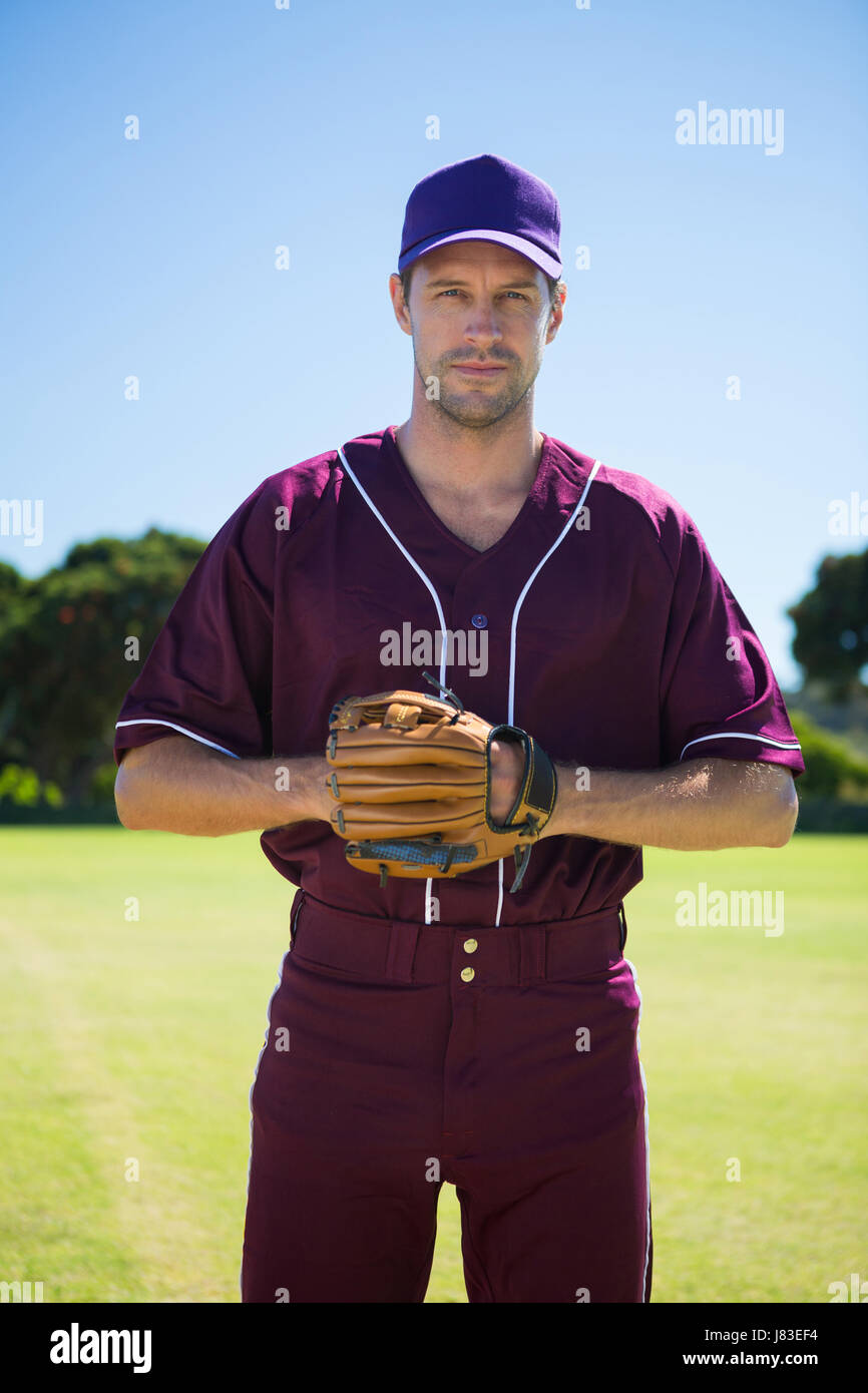 Portrait of confident baseball pitcher standing on field against clear ...