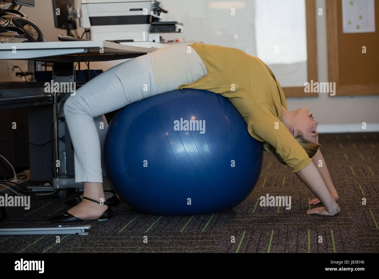 Executive performing stretching exercise on fitness ball in office ...