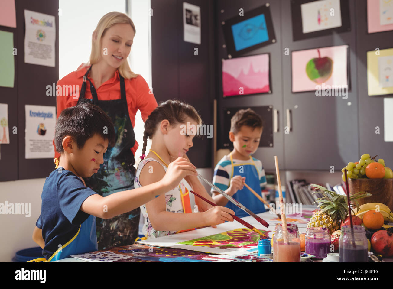 Teacher assisting schoolkids in drawing class at school Stock Photo - Alamy