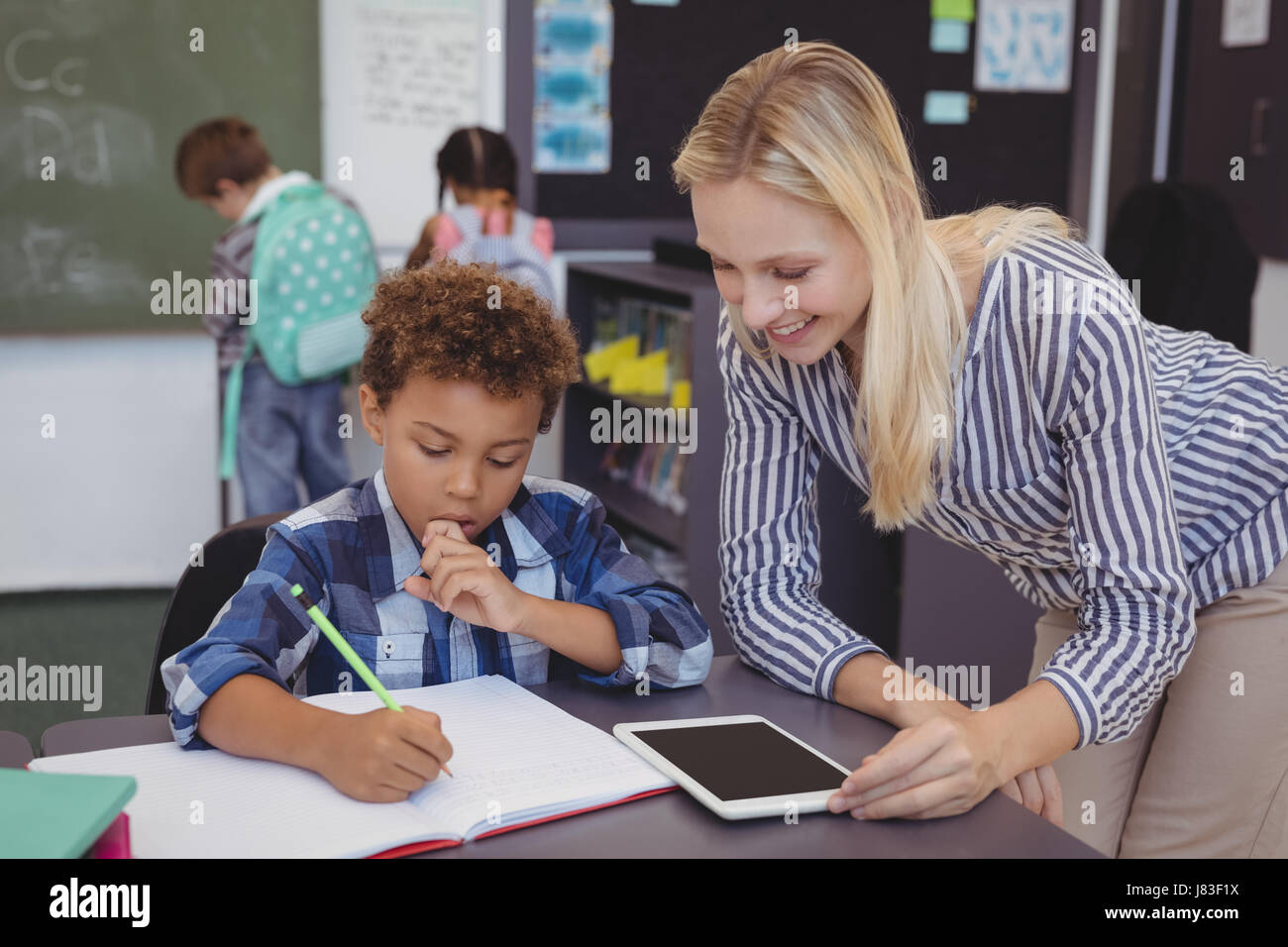 Teacher helping schoolboy with his homework in classroom at school ...