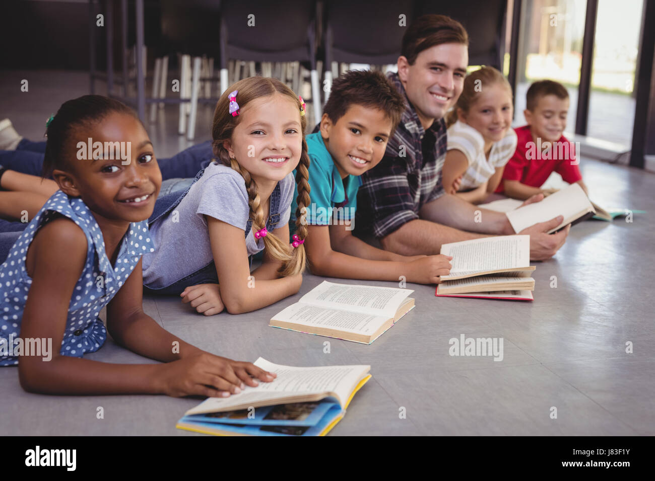 Portrait of teacher and schoolkids lying on floor while reading books ...
