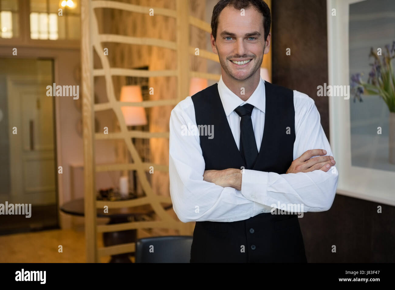Portrait of confident waiter with arms crossed standing in restaurant ...