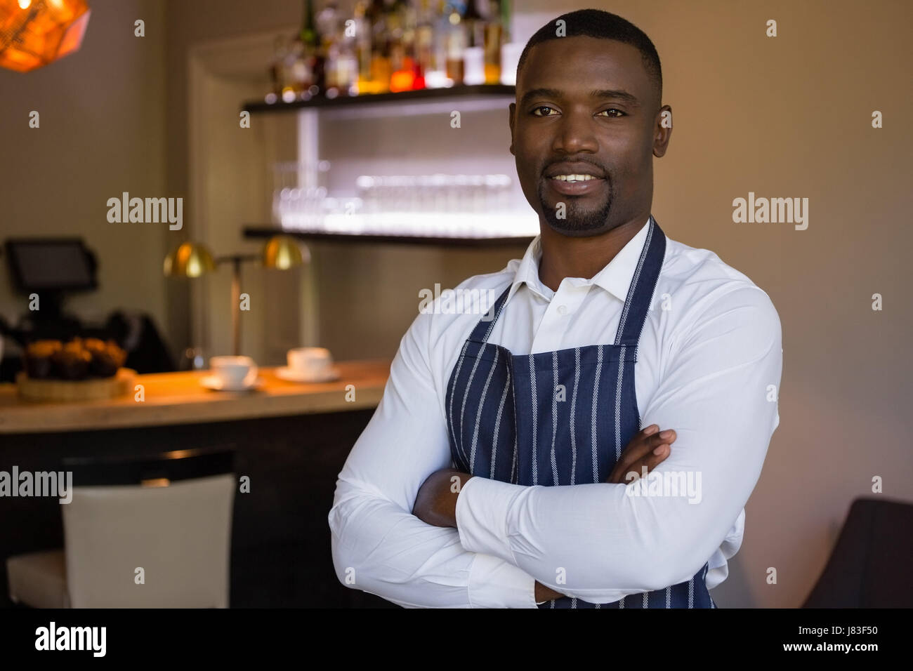 Portrait of confident waiter standing with arms crossed in restaurant ...