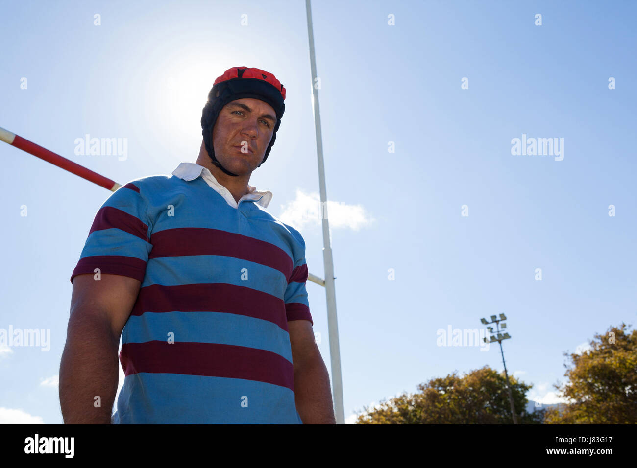 Low angle portrait of rugby player wearing helmet by goal post against ...