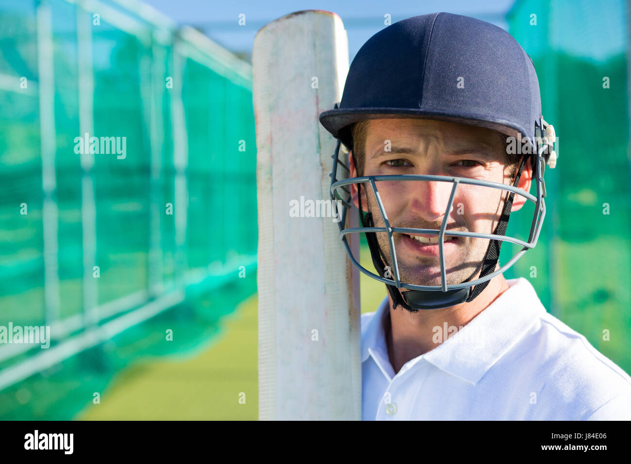 Portrait of confident cricket player wearing helmet holding bat at ...