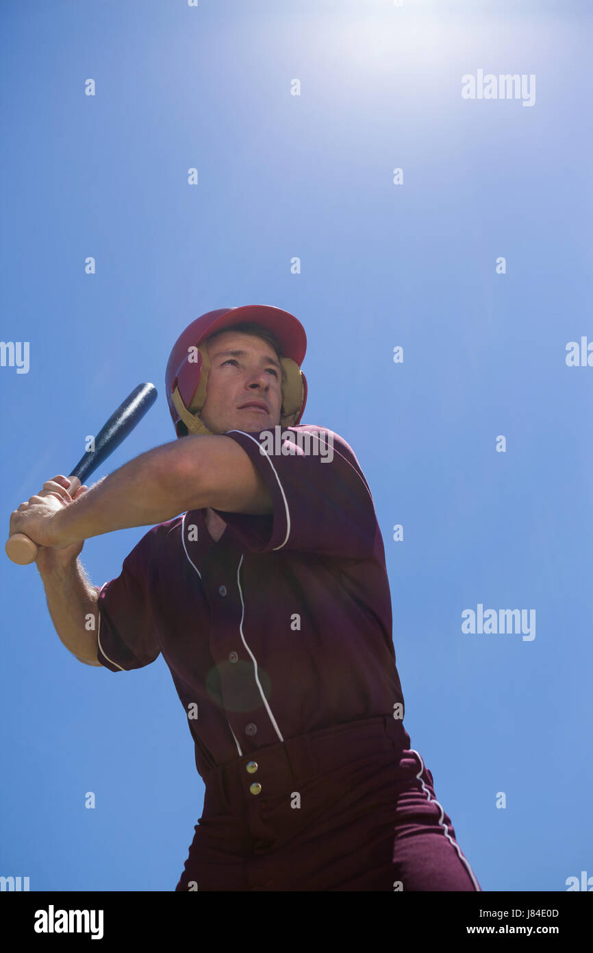 Low angle view of confident player with baseball bat against blue sky ...