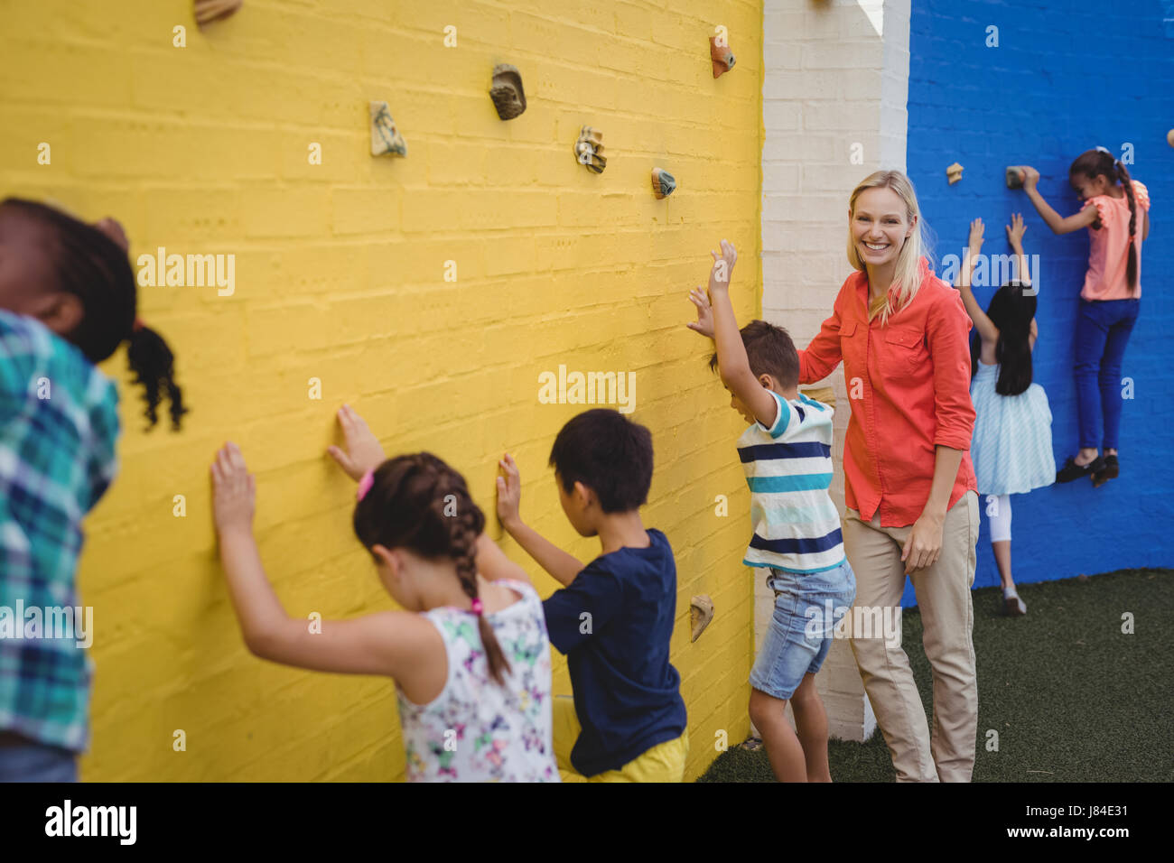 Trainer assisting kids in climbing wall in school Stock Photo - Alamy