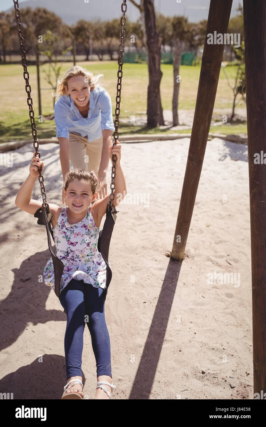 Trainer pushing girl on swing at school playground Stock Photo - Alamy