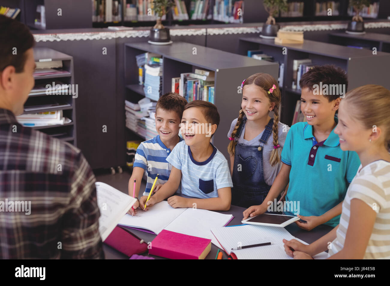 Happy schoolkids interacting with teacher in library at school Stock ...