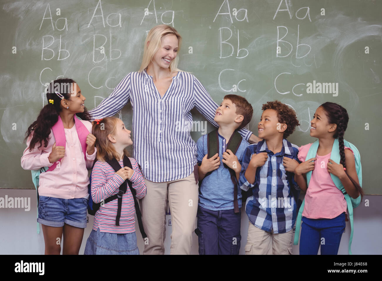 Happy teacher standing with schoolkids in classroom at school Stock ...