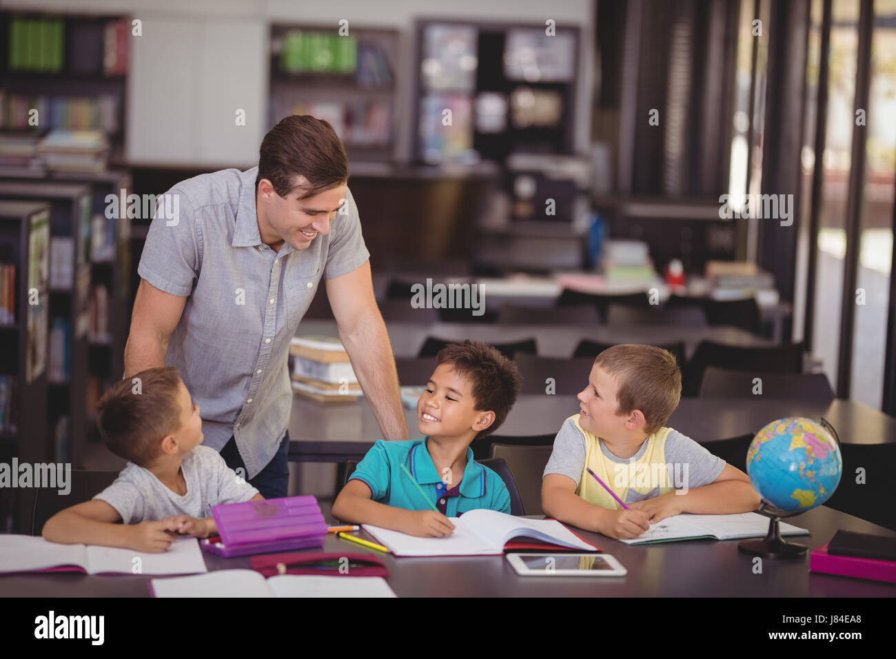 Teacher helping schoolkids with their homework in library at school ...