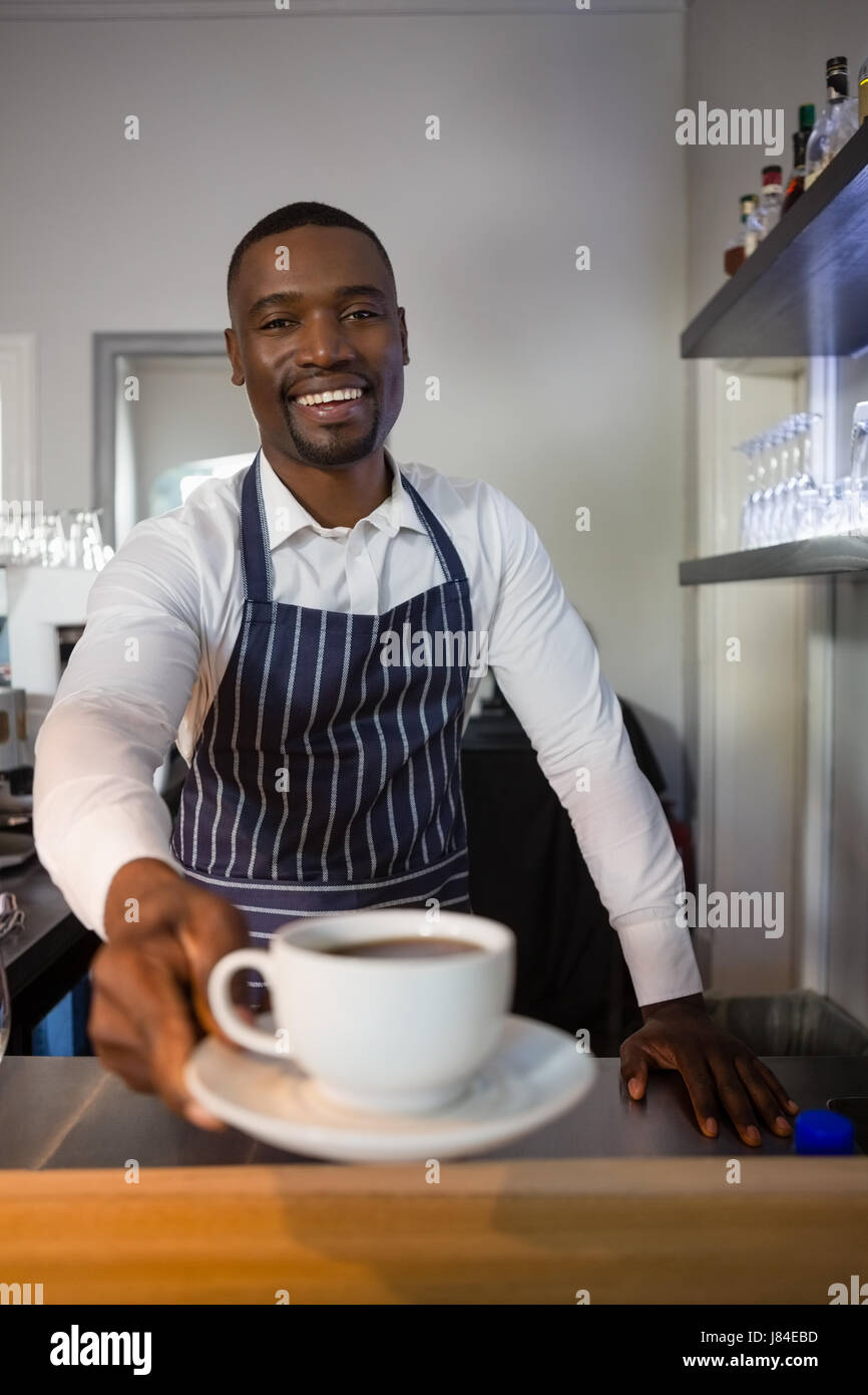 Portrait of smiling waiter giving coffee at counter in cafe Stock Photo ...