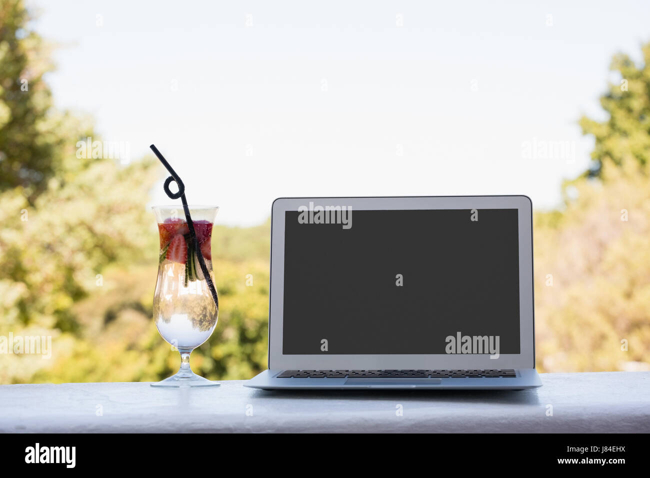Close up of laptop and cocktail drink on retaining wall at restaurant ...