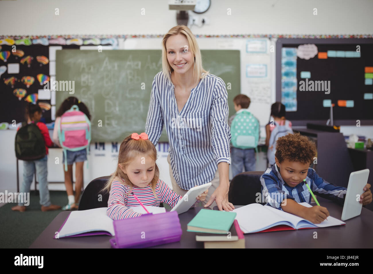 Teacher helping schoolkids with their homework in classroom at school ...