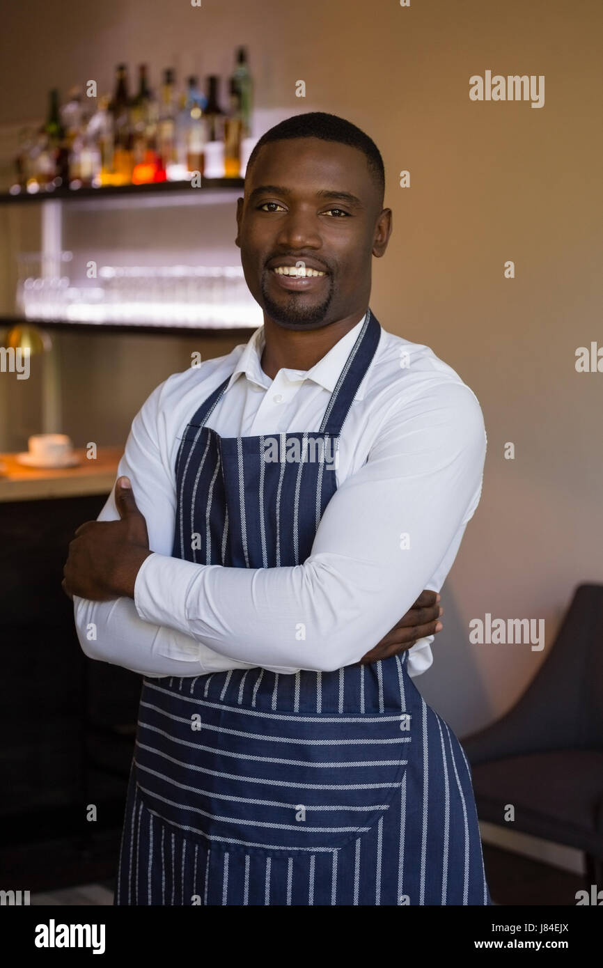 Portrait of smiling confident waiter standing with arms crossed in ...