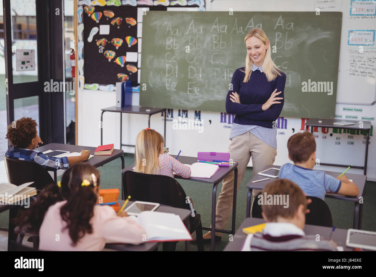 Teacher helping schoolkids with their homework in classroom at school ...