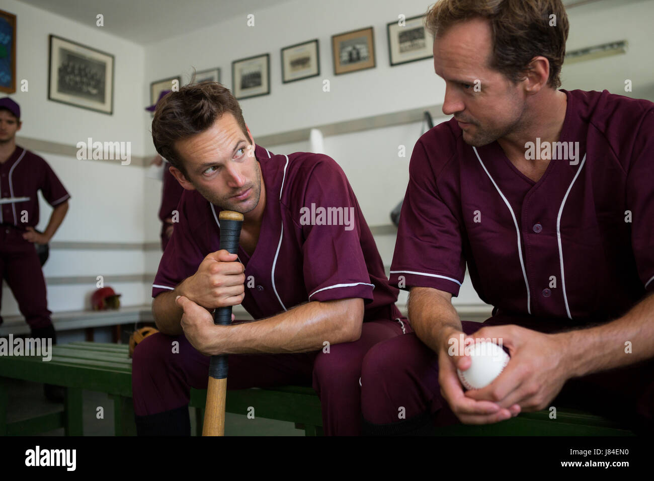 Baseball players sitting together on bench in locker room Stock Photo ...