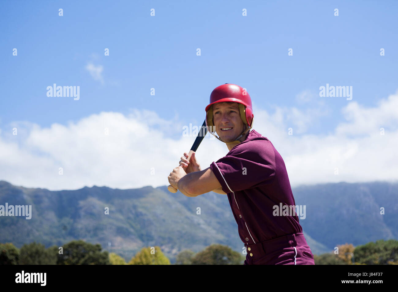 Smiling baseball player with bat standing against mountains Stock Photo ...