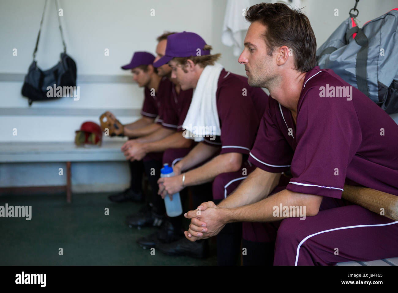 Side view of tired basball players sitting on bench at locker room ...