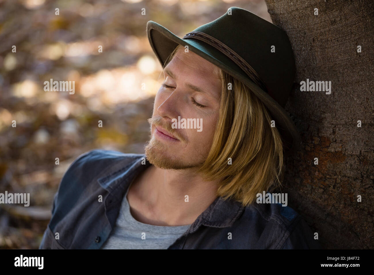Young man resting against a tree in the park Stock Photo - Alamy