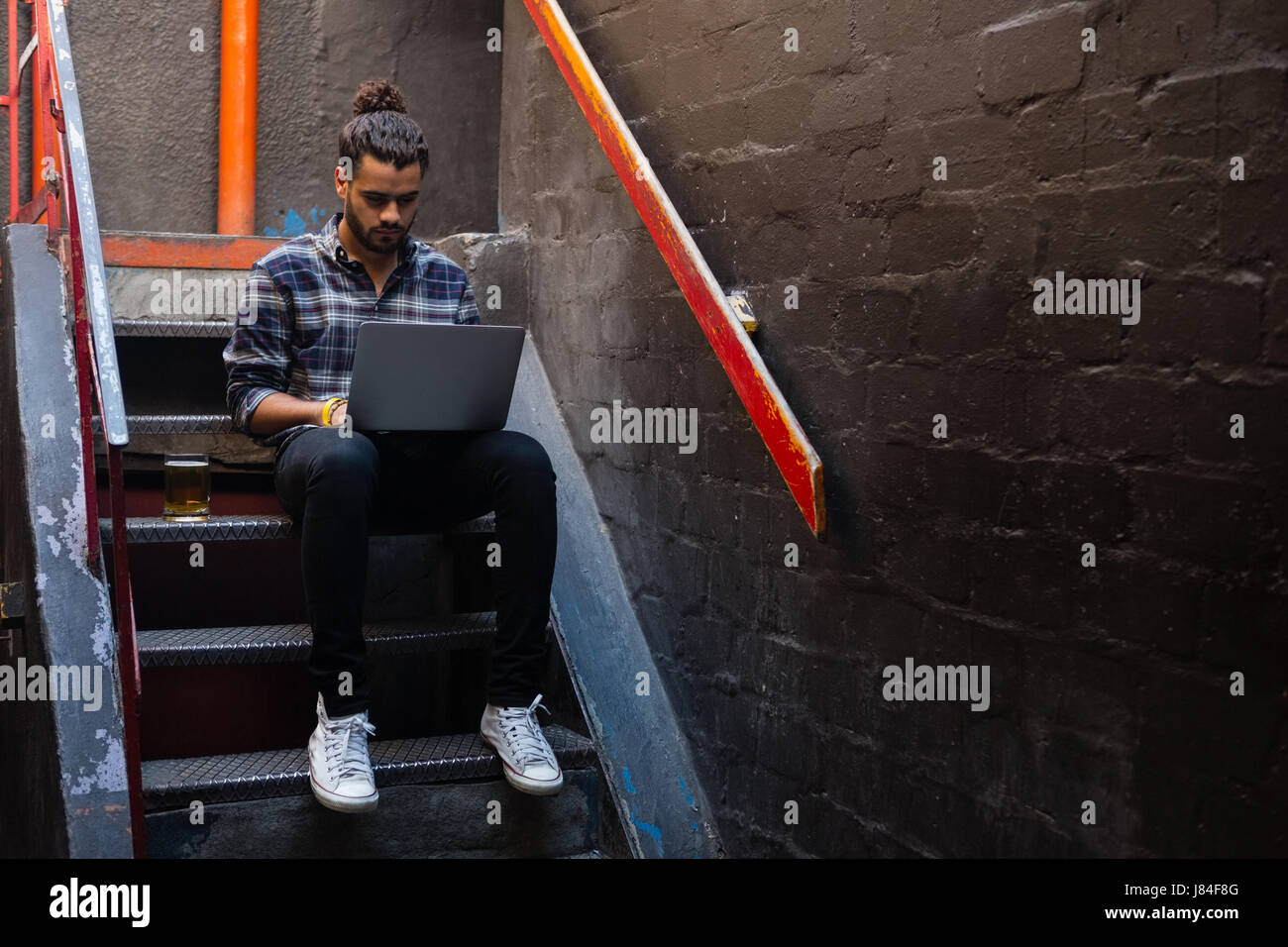 Man using laptop on staircase of bar Stock Photo - Alamy