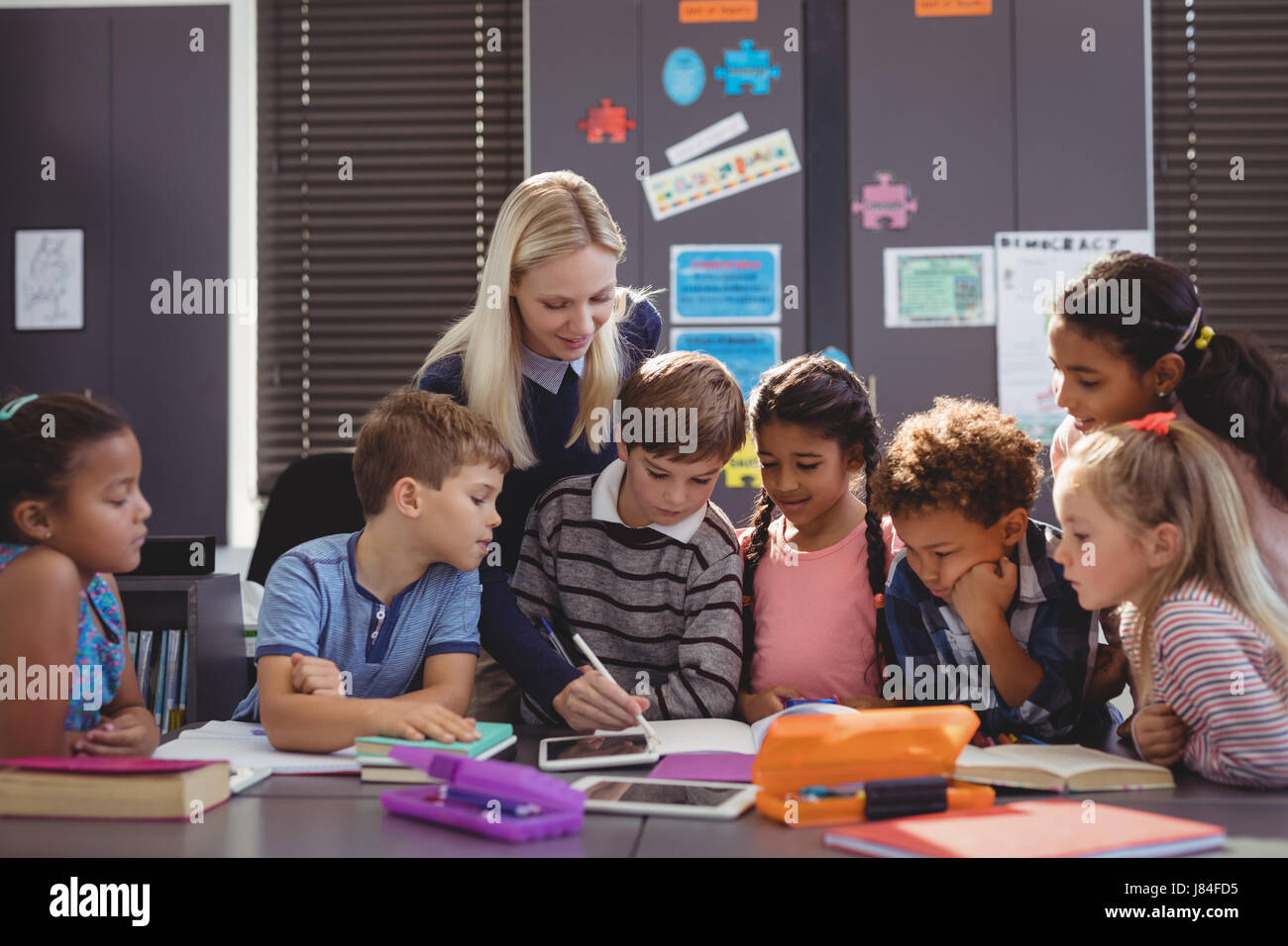 Teacher helping schoolgirl with her homework in classroom at school ...