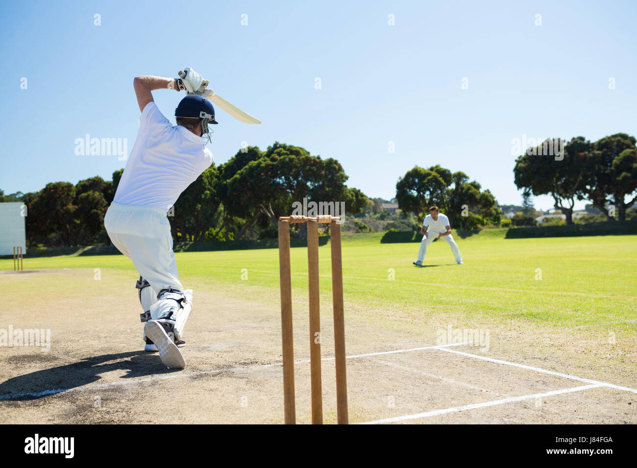Rear view of player batting while playing cricket on field against ...