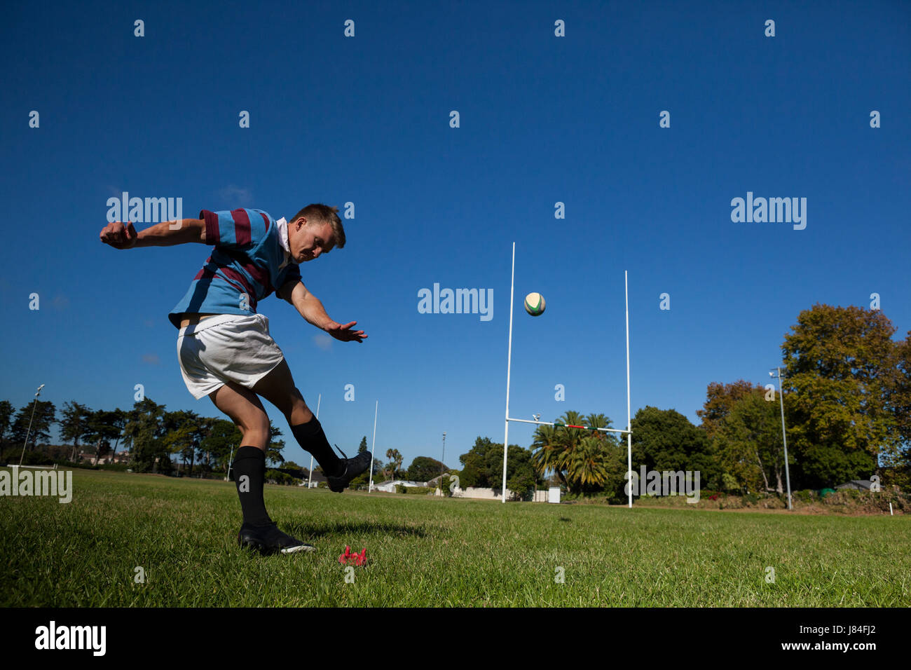 Low angle view of rugby player kicking ball for goal against clear blue ...