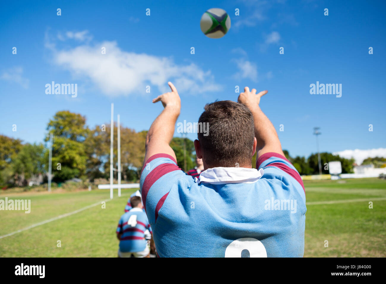 Rear view of player throwing ball while playing rugby at field on sunny ...