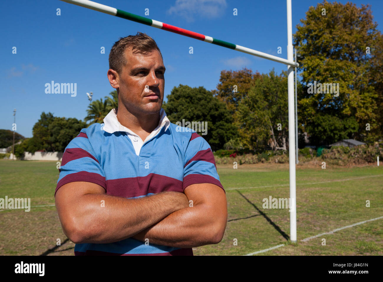Thoughtful rugby player with arms crossed standing at playing field on ...