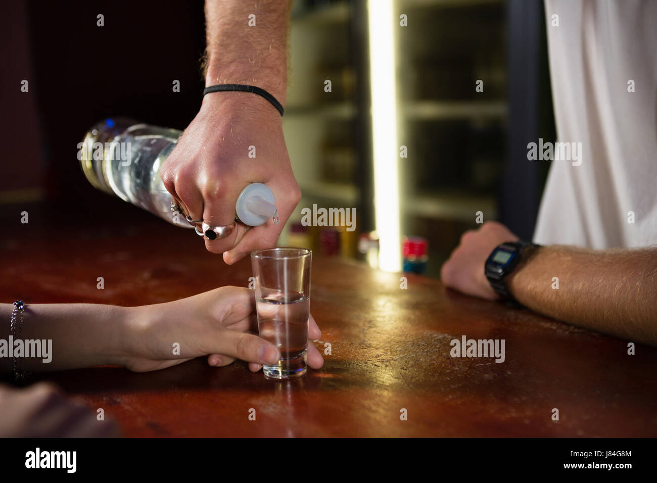 Mid section of bartender serving tequila to customer at bar counter ...