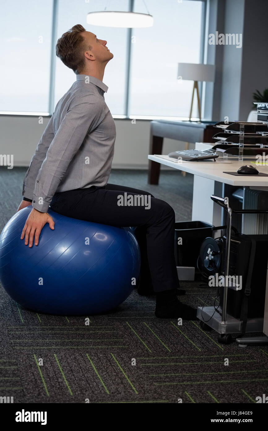 Executive performing stretching exercise on fitness ball in office ...