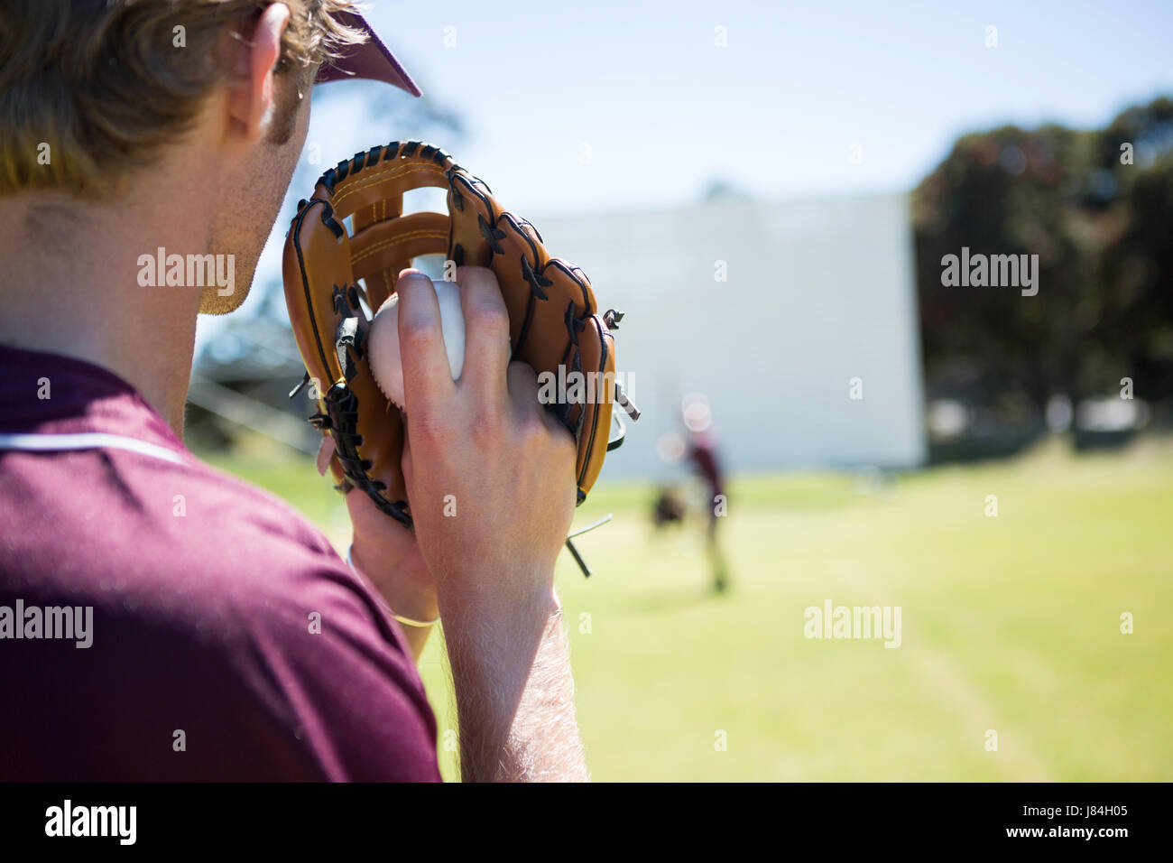 Baseball pitcher holding ball in glove at playing field on sunny day ...