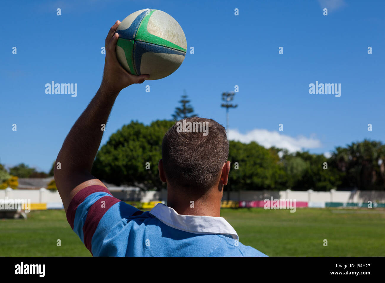 Rear view of rugby player holding ball at playing field during sunny ...
