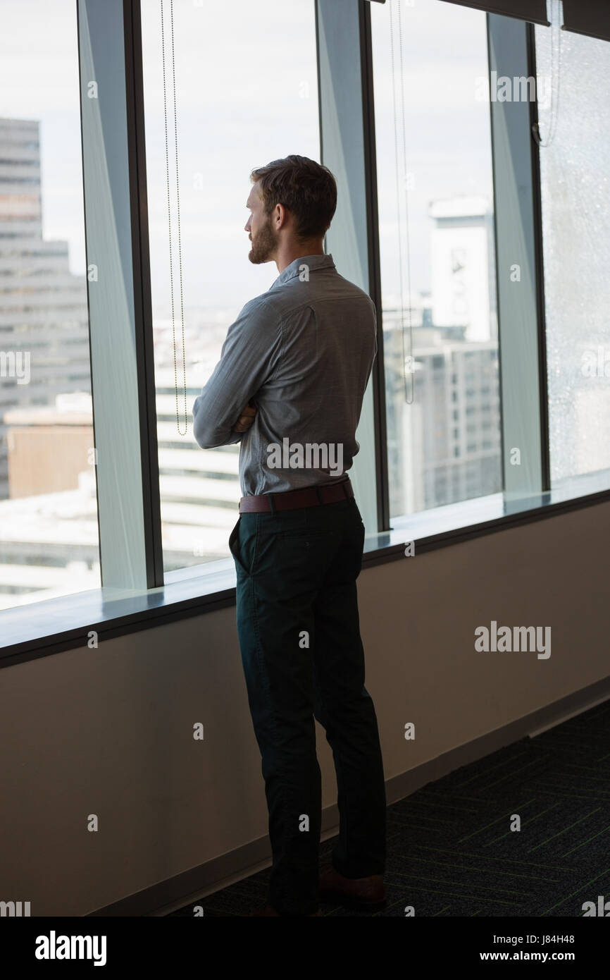 Thoughtful male executive looking through window in office Stock Photo ...