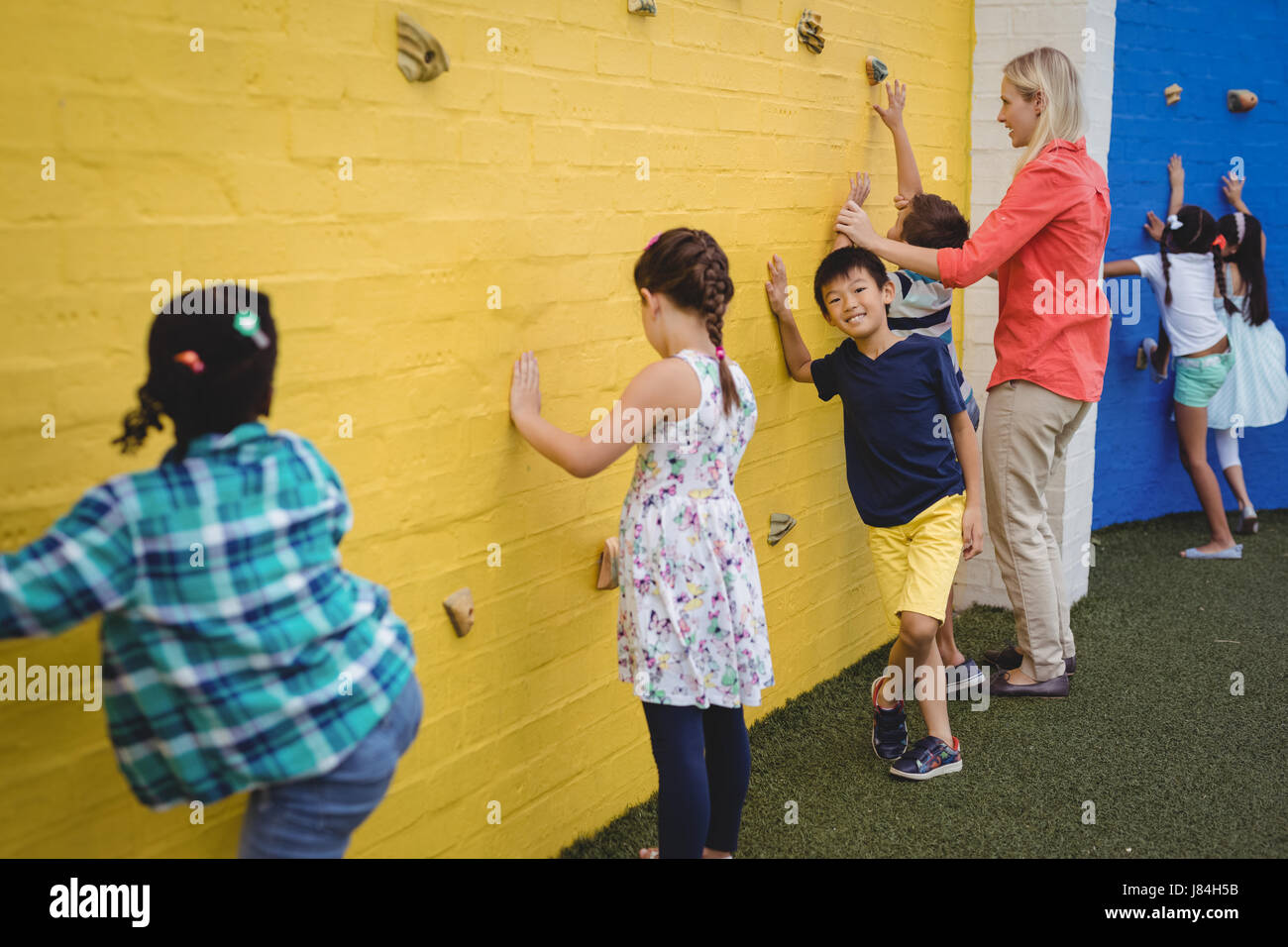 Trainer assisting kids in climbing wall in school Stock Photo - Alamy