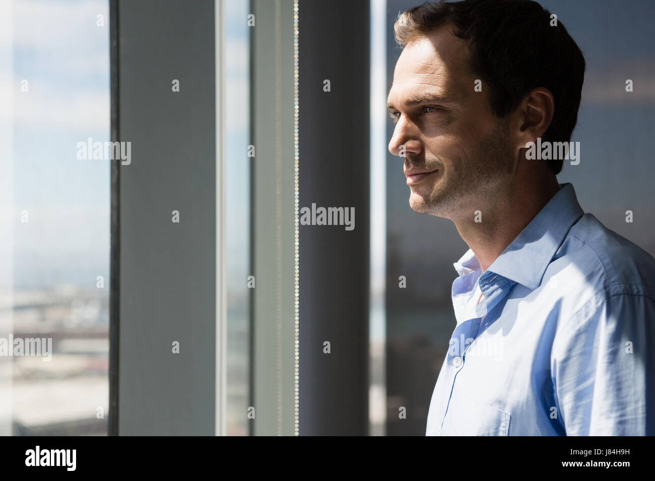 Thoughtful male executive looking through window in office Stock Photo ...