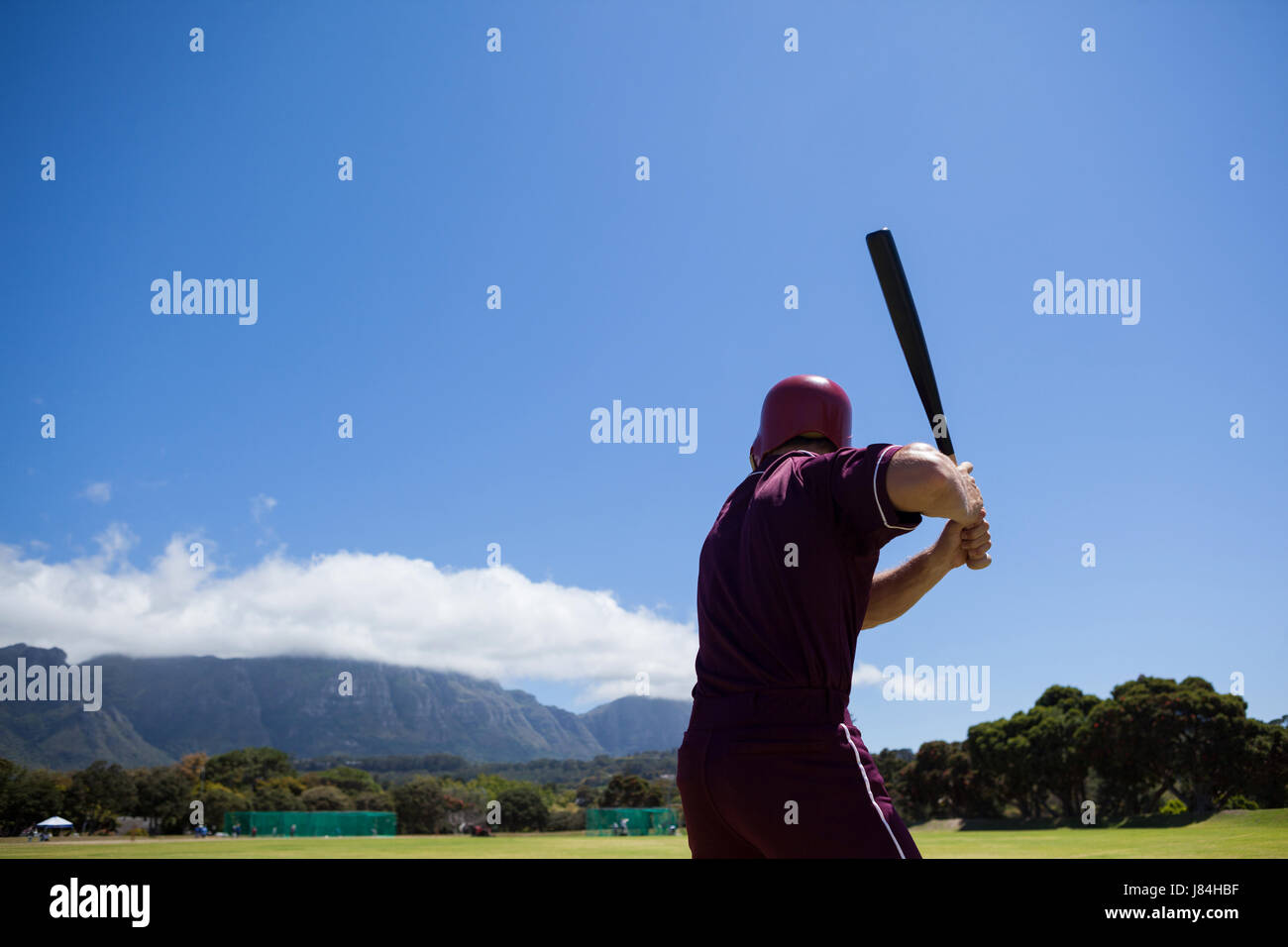 Rear view of baseball player with bat standing at field against blue ...