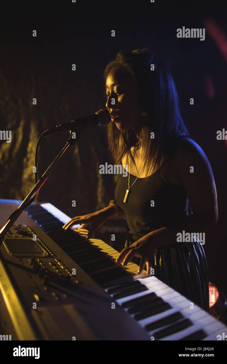 Confident female playing piano while singing in illuminated nightclub ...