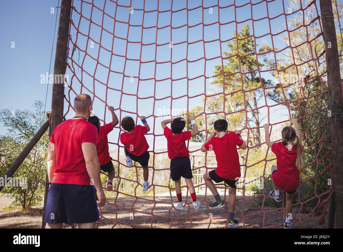 Trainer instructing kids in net climbing during obstacle course ...