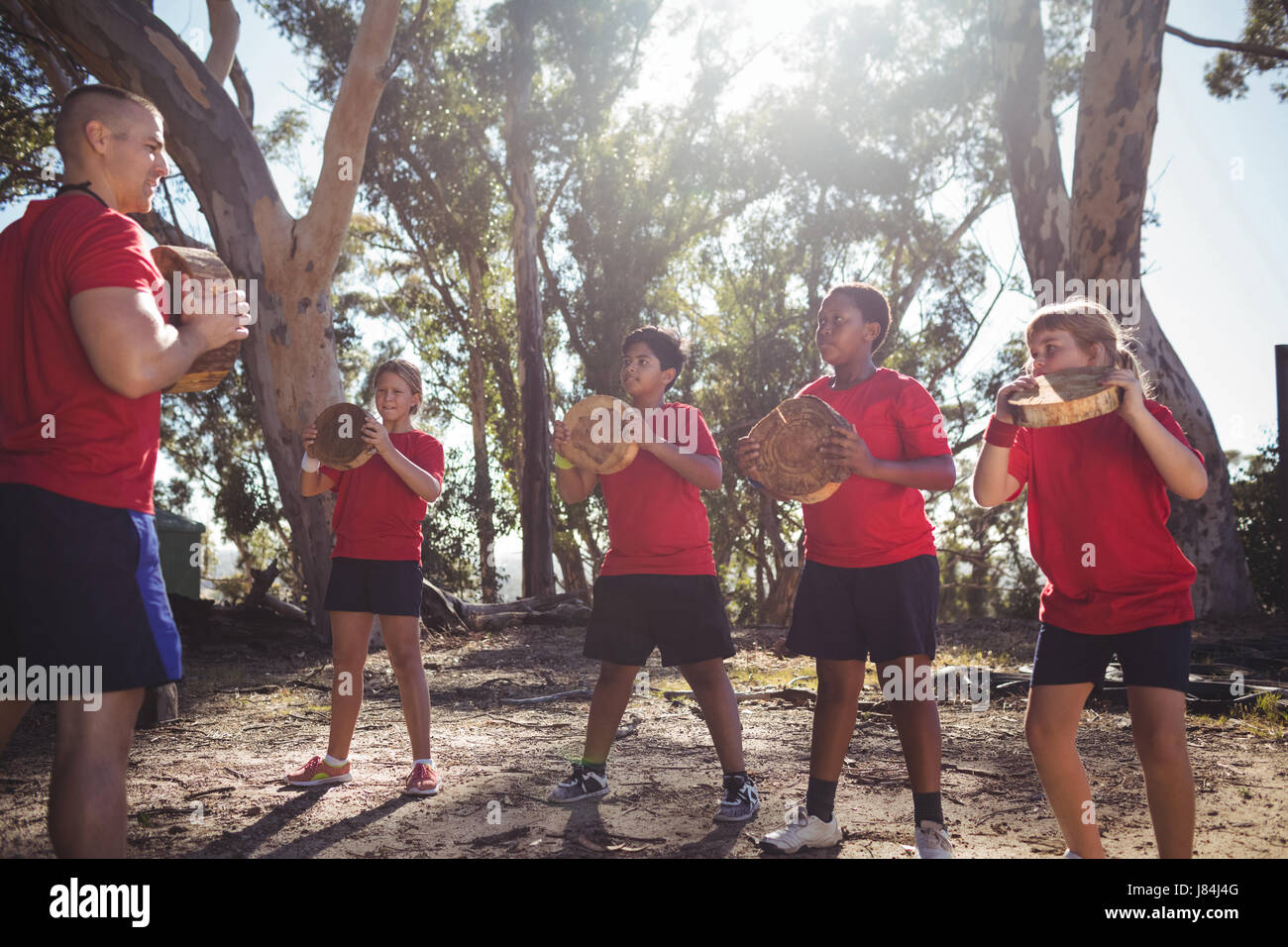 Trainer and kids carrying wooden logs during obstacle course training ...