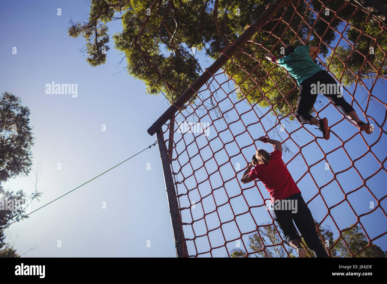 Group of fit woman climbing a net during obstacle course training in ...