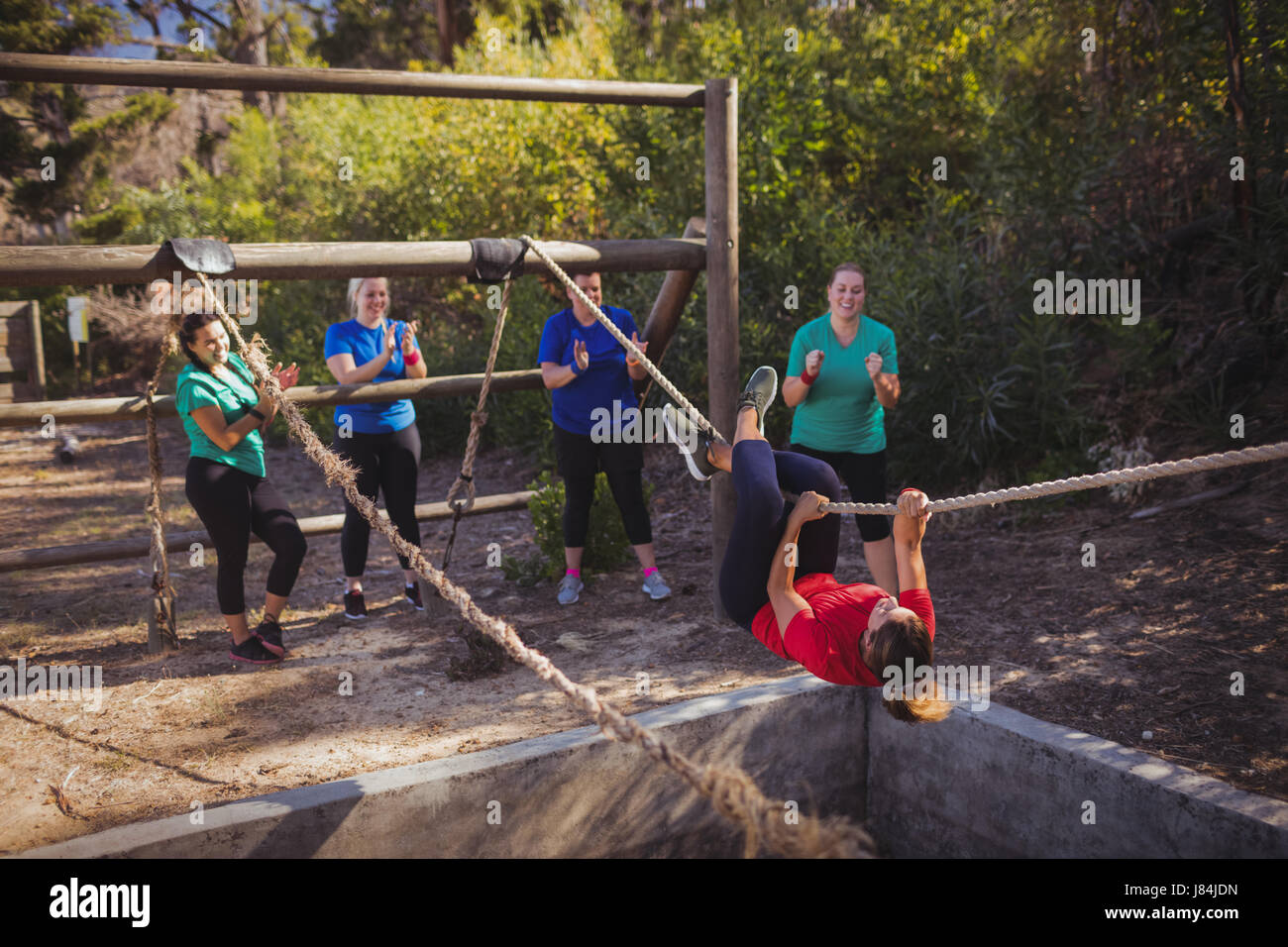 Fit woman climbing a rope during obstacle course training in the boot ...