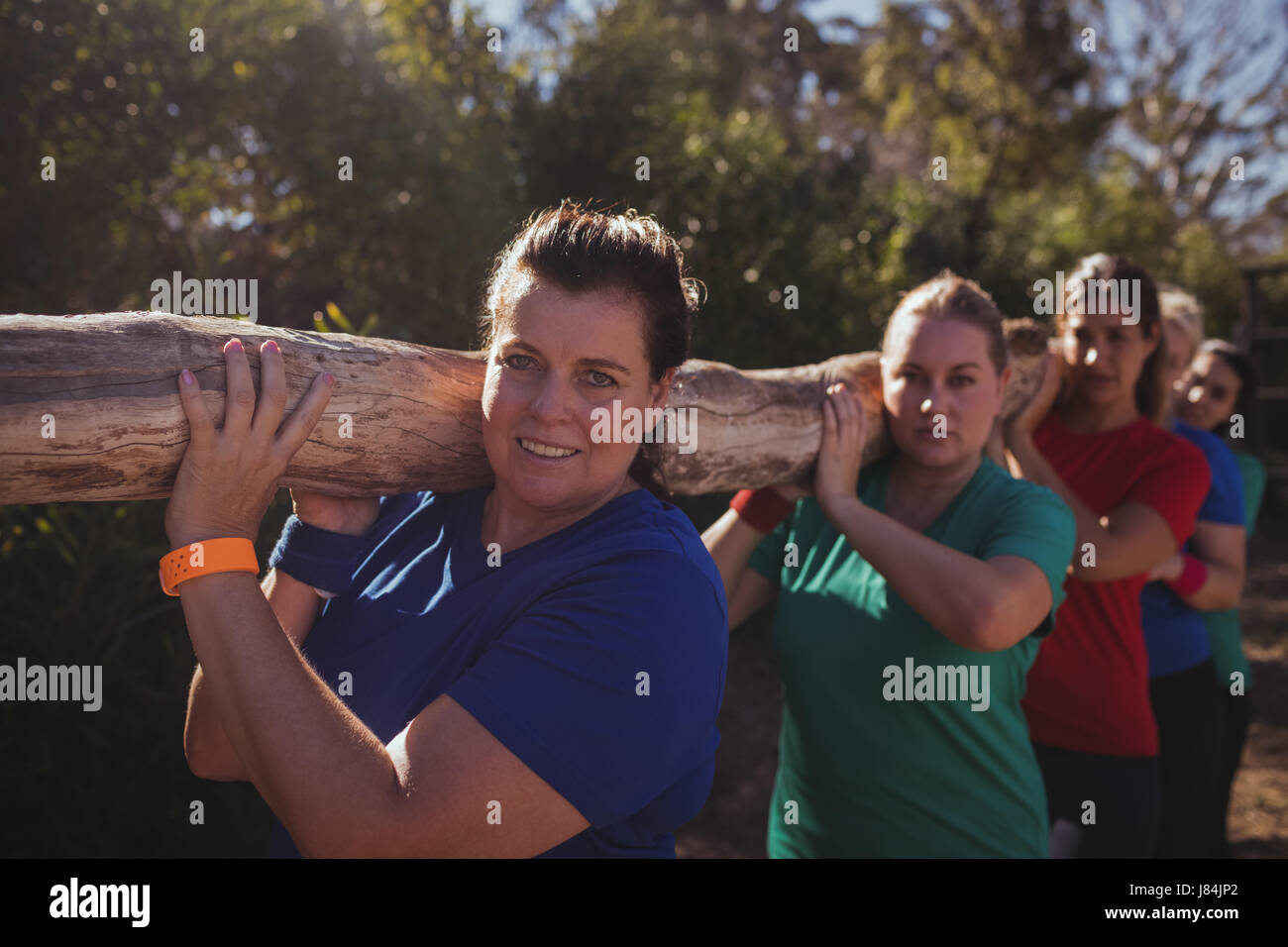 Group of fit women carrying a heavy wooden log during obstacle course ...